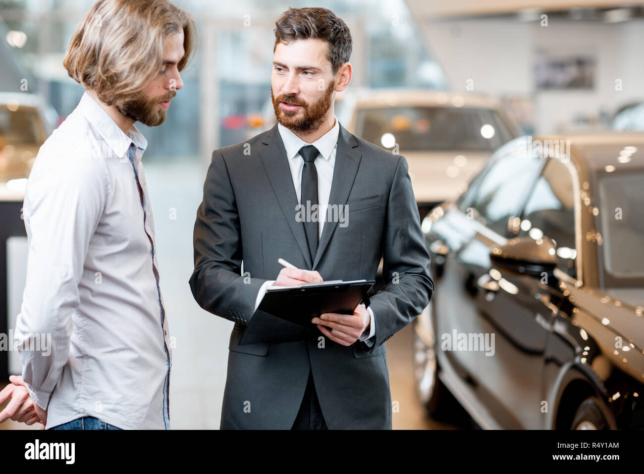 Professional car salesman with male client signing documents standing ...