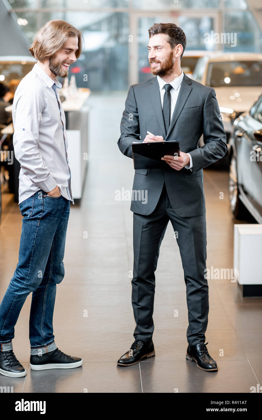 Professional car salesman with male client signing documents standing ...