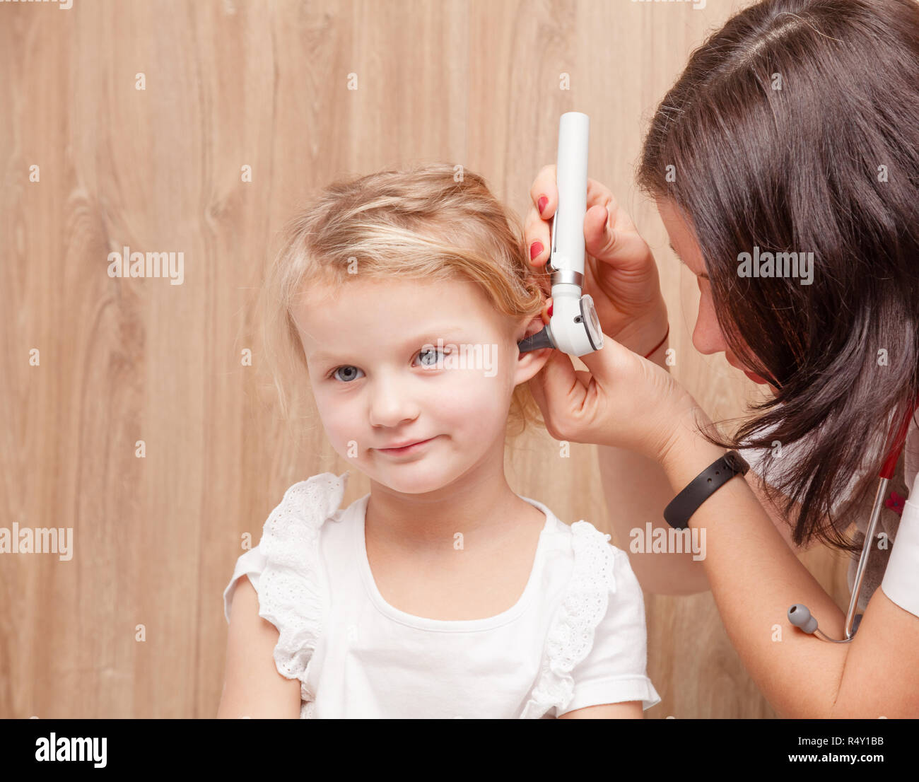 Female pediatrician examines little girl's ear. Doctor using a otoscope ...