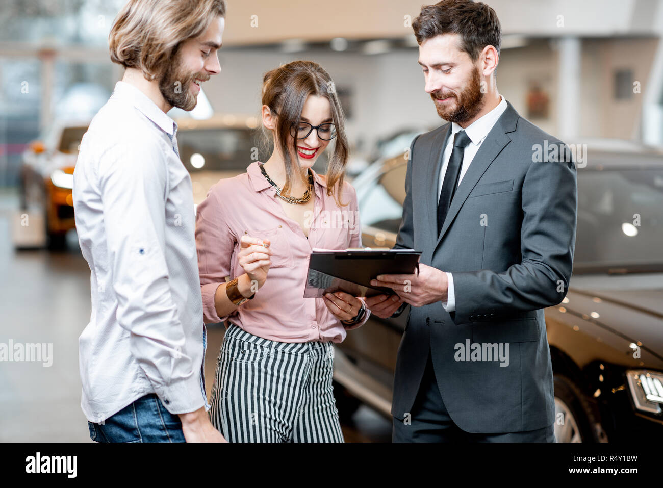 Handsome male dealer selling to a young couple clients a new car ...
