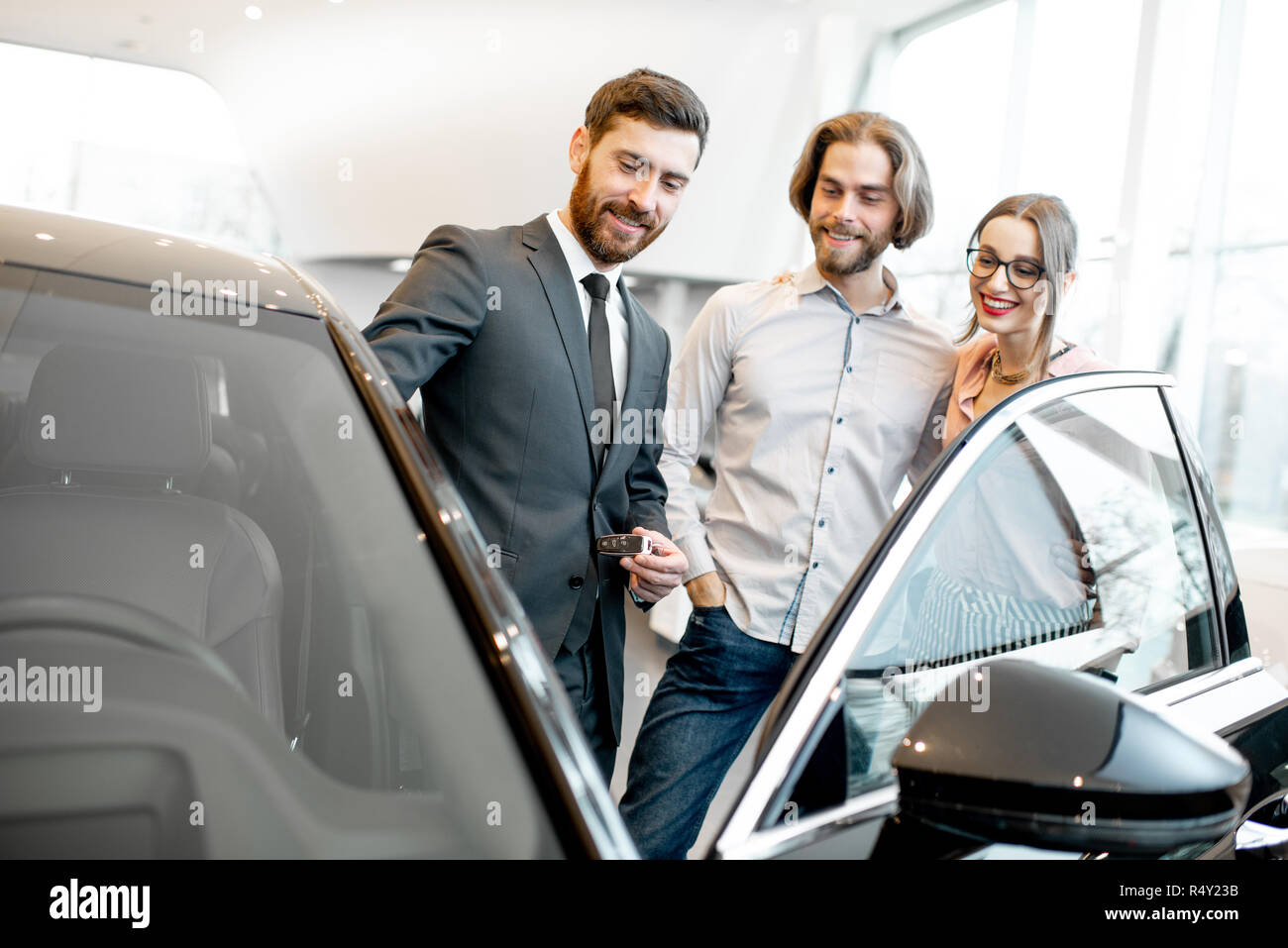 Car salesman showing car interior to a young couple clients in the ...