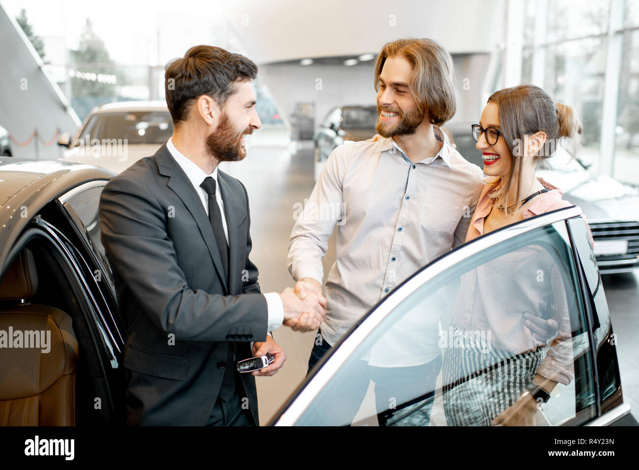Car salesman showing car interior to a young couple clients in the ...
