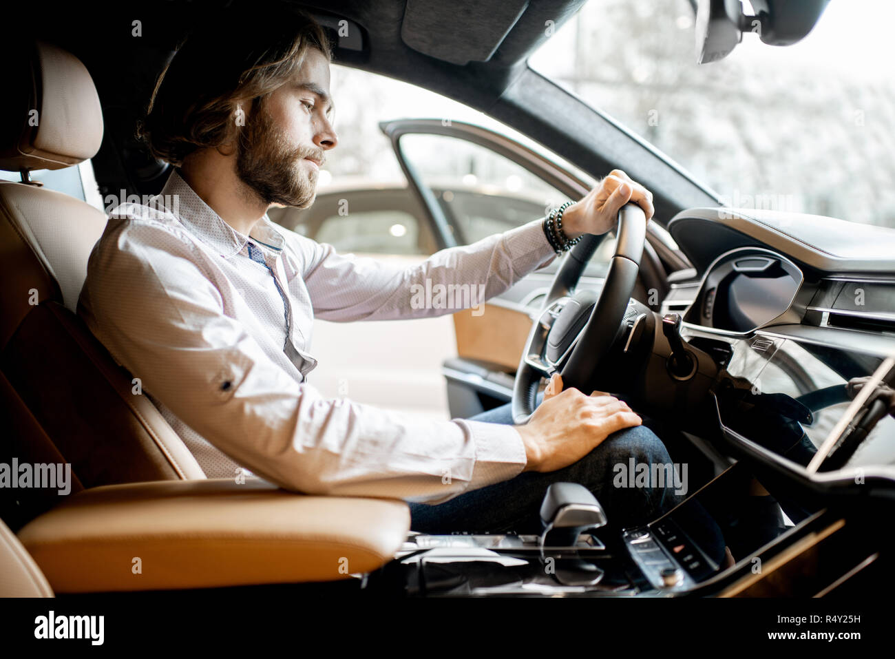Young handsome man trying a new car sitting in the luxury car interior ...