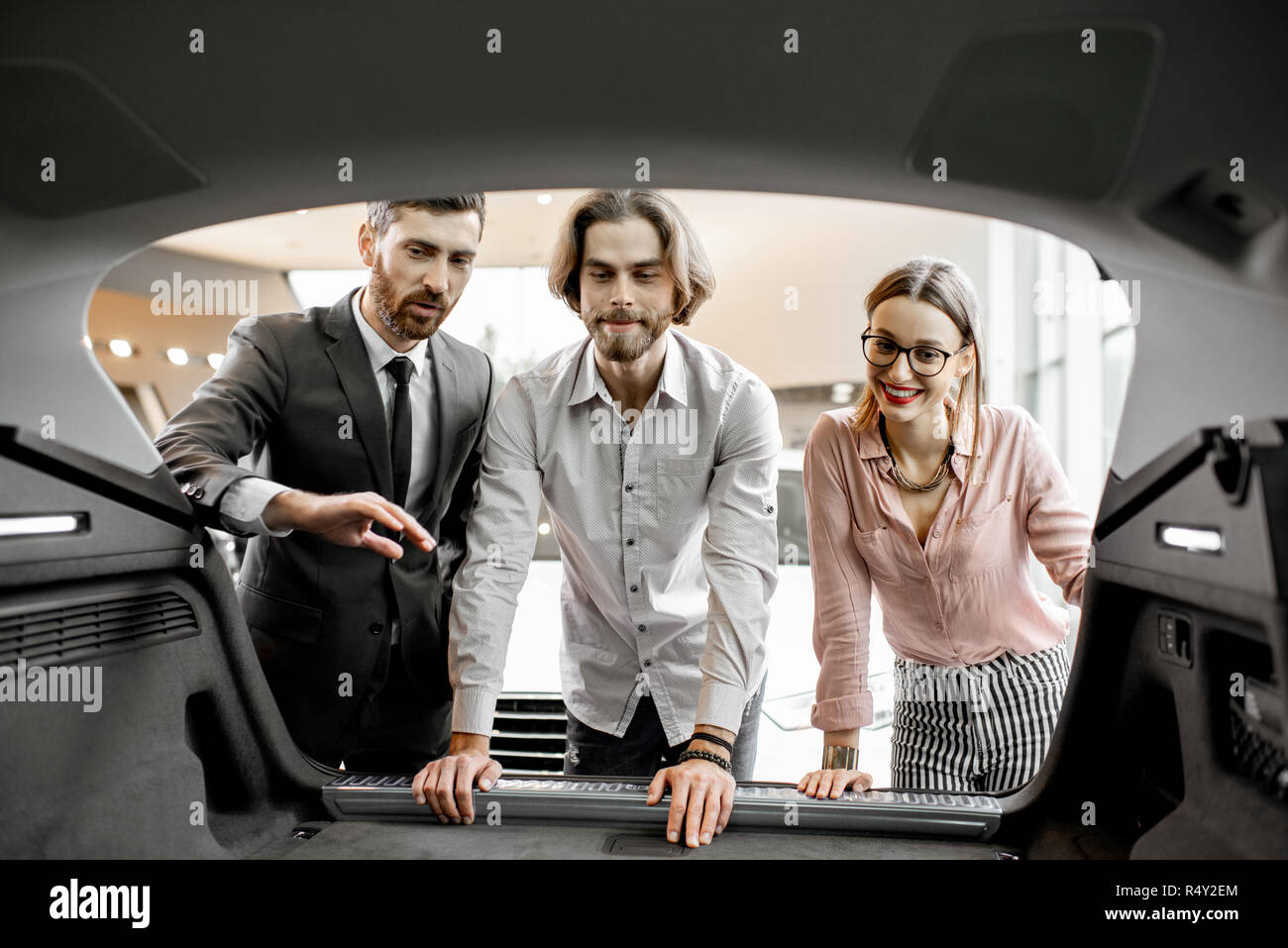 Salesman showing spacious trunk of a new car for a young couple clients ...
