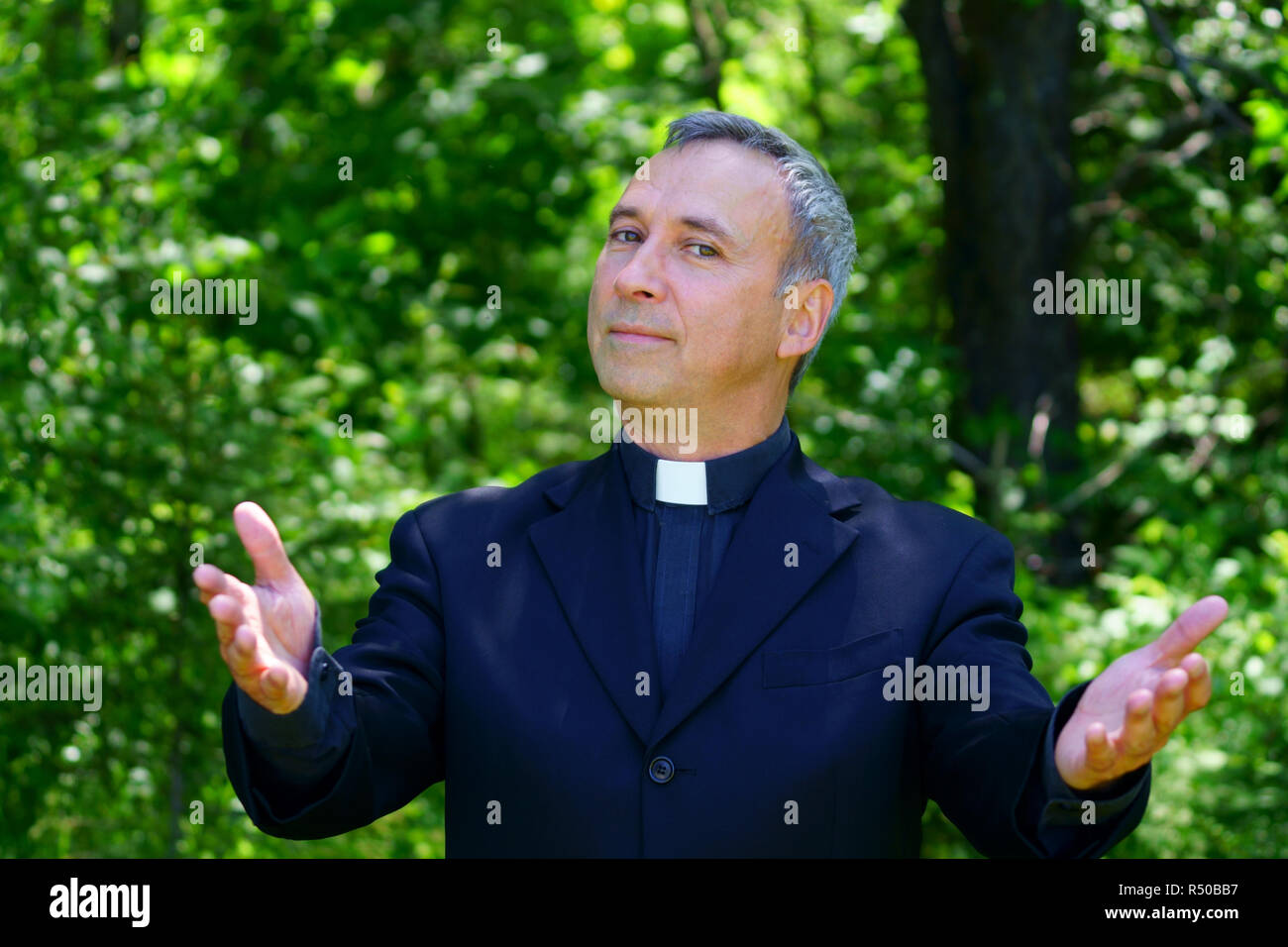 A good looking catholic priest is walking in the forest. Standing and ...