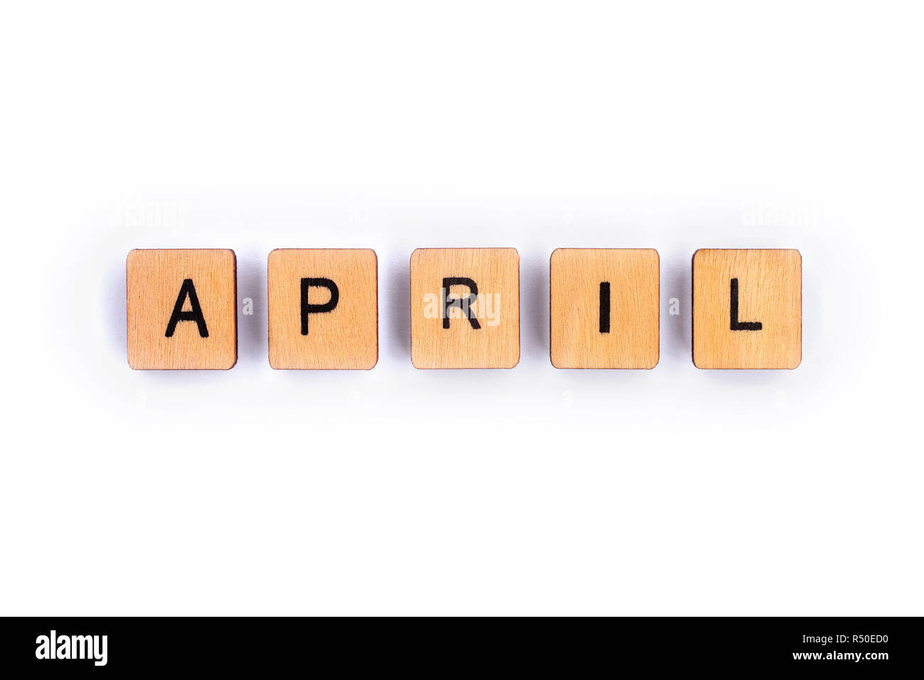 APRIL, spelt with wooden letter tiles over a plain white background ...
