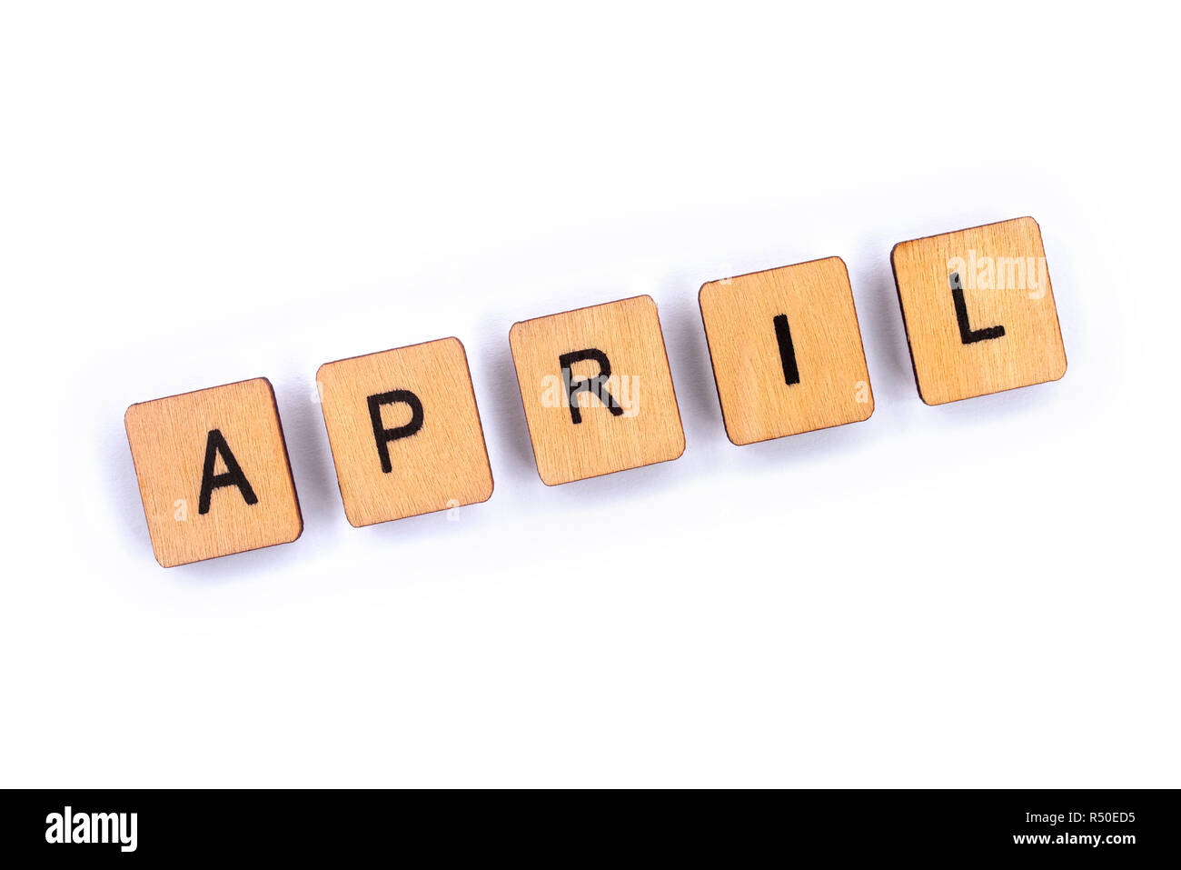 APRIL, spelt with wooden letter tiles over a plain white background ...