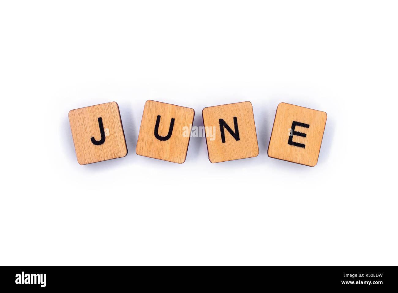 JUNE, spelt with wooden letter tiles over a plain white background ...