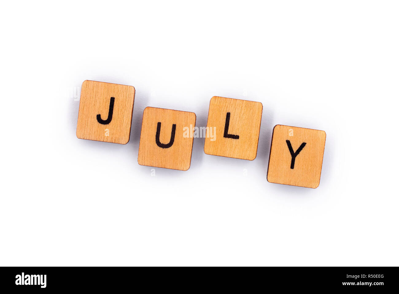 JULY, spelt with wooden letter tiles over a plain white background ...