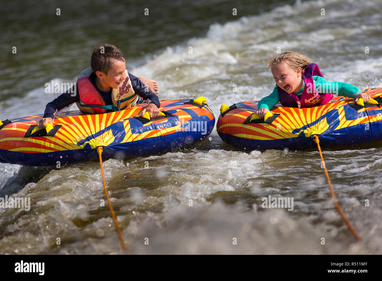 Front view of two children having fun tubing on river Stock Photo - Alamy