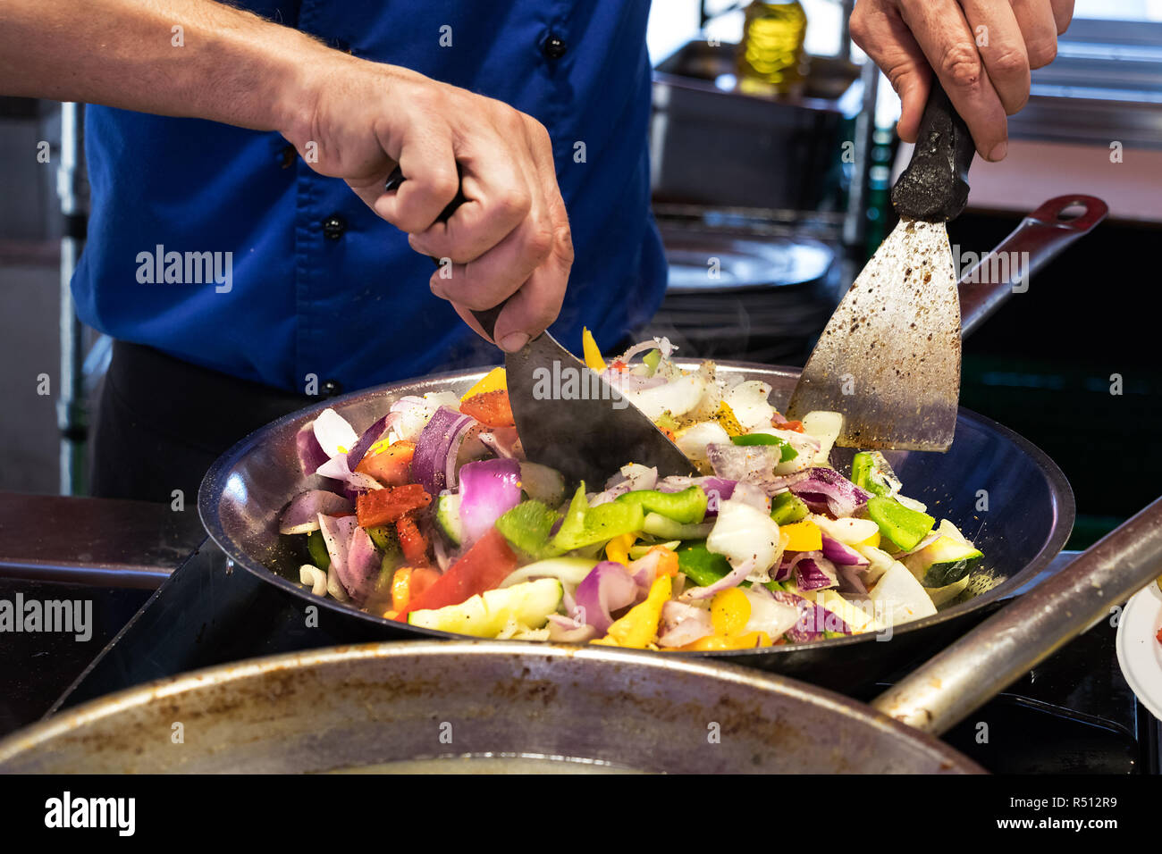 A male cooker frying food vegetables in cooking pan with spatulas Stock ...
