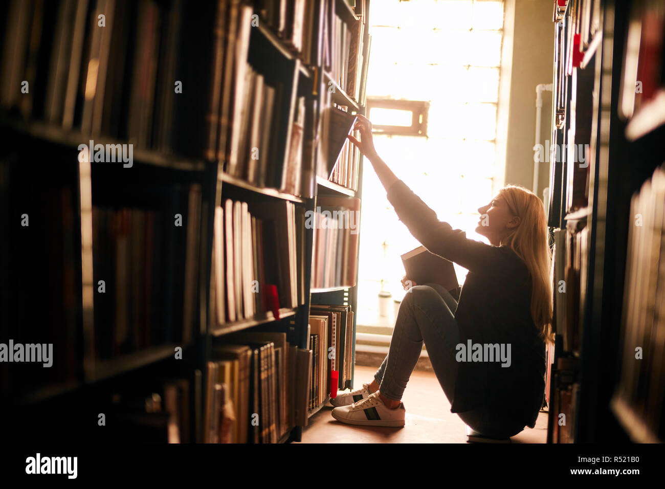 Young girl sitting on the floor in traditional library at bookshelves ...