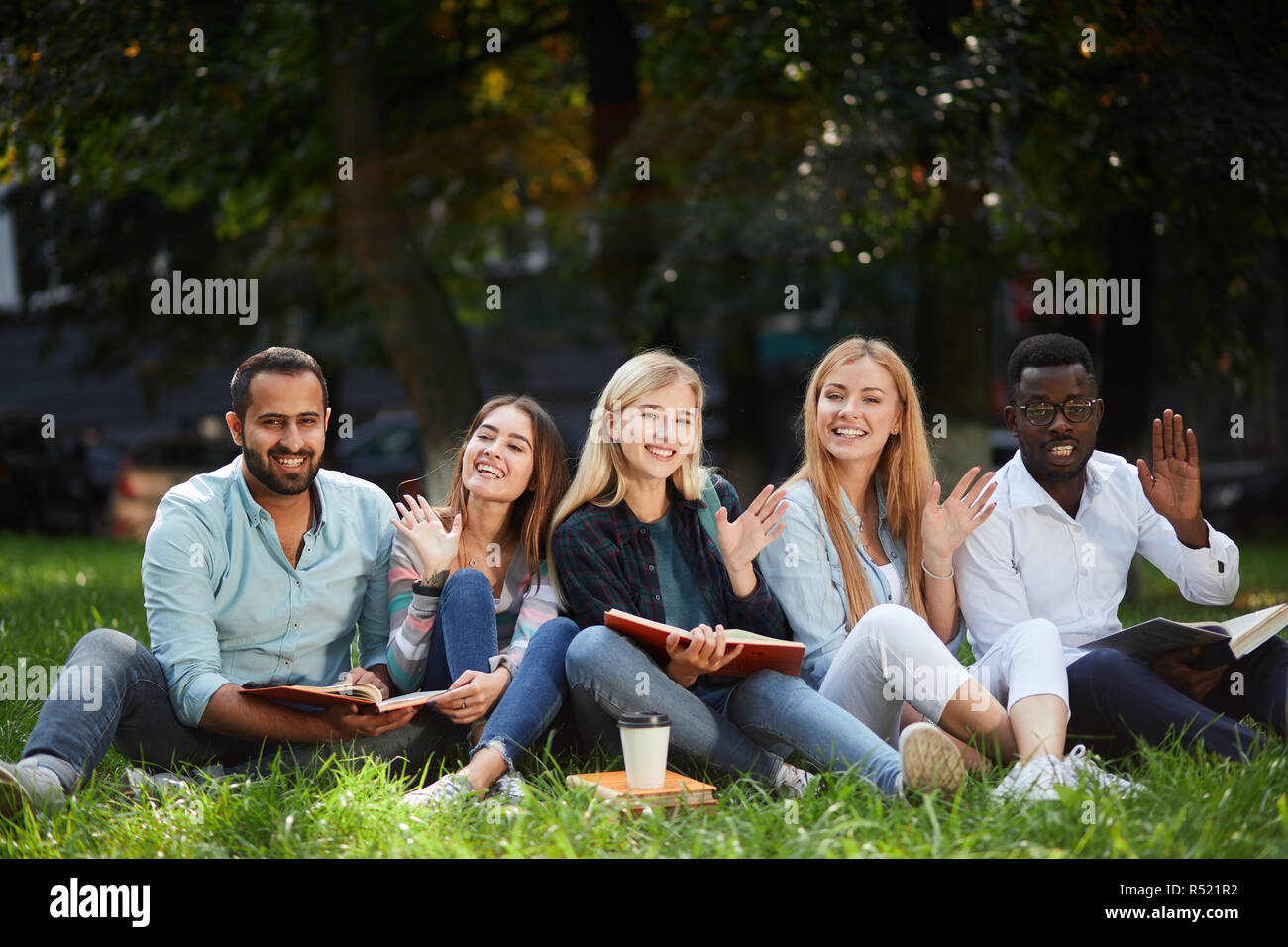 Mixed-race group of students sitting together on green lawn of ...