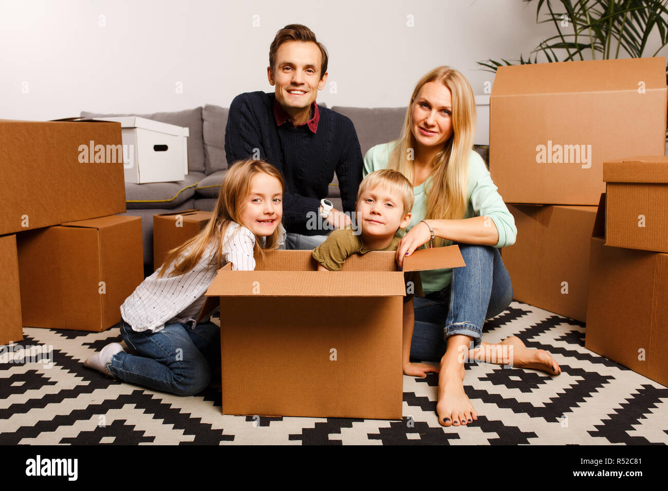Photo of happy parents with children sitting on floor among cardboard ...