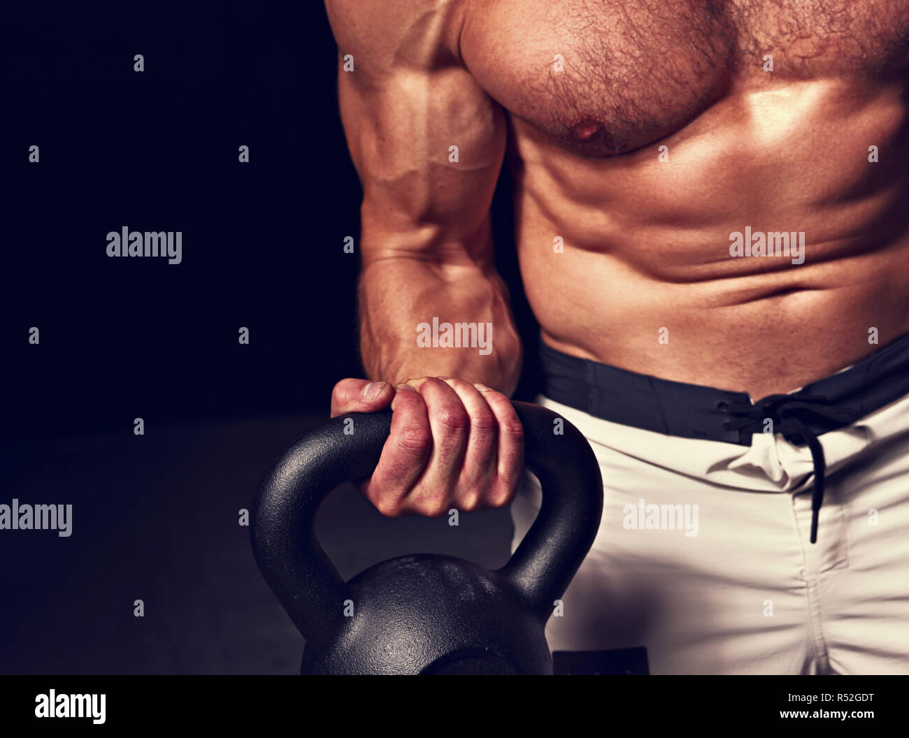 Strong athletic fitness man doing the exercises with kettlebell on dark ...