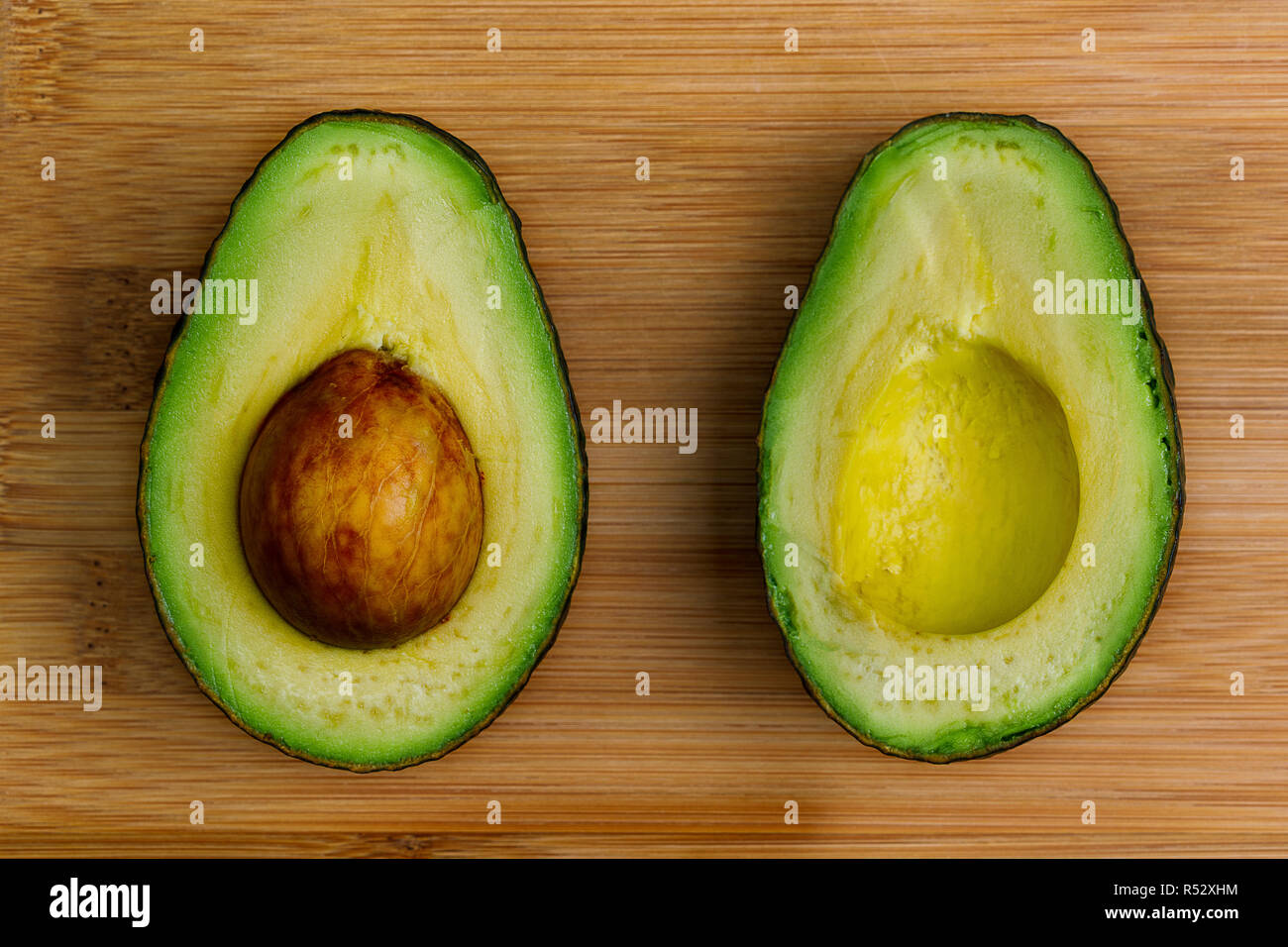 Two halves of an avocado face up with the pit still in place, on a ...