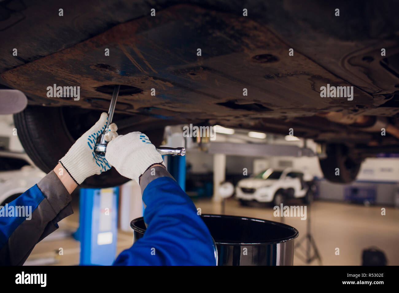 Young mechanic fixing wheel under car in service Stock Photo - Alamy