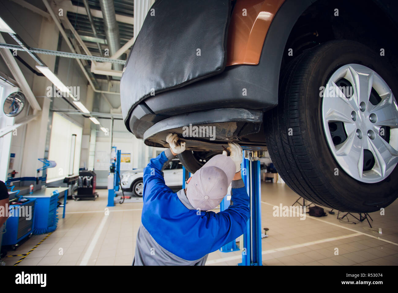 Young mechanic fixing wheel under car in service Stock Photo - Alamy