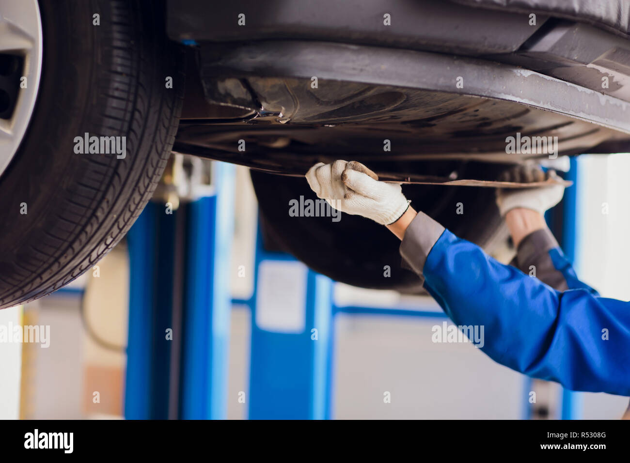 Young mechanic fixing wheel under car in service Stock Photo - Alamy
