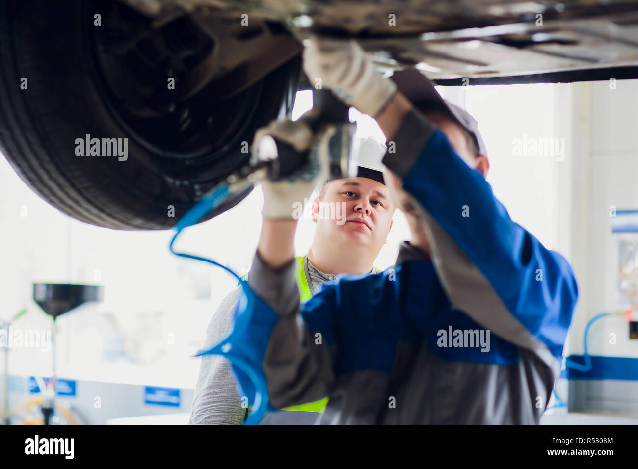 Young mechanic fixing wheel under car in service Stock Photo - Alamy