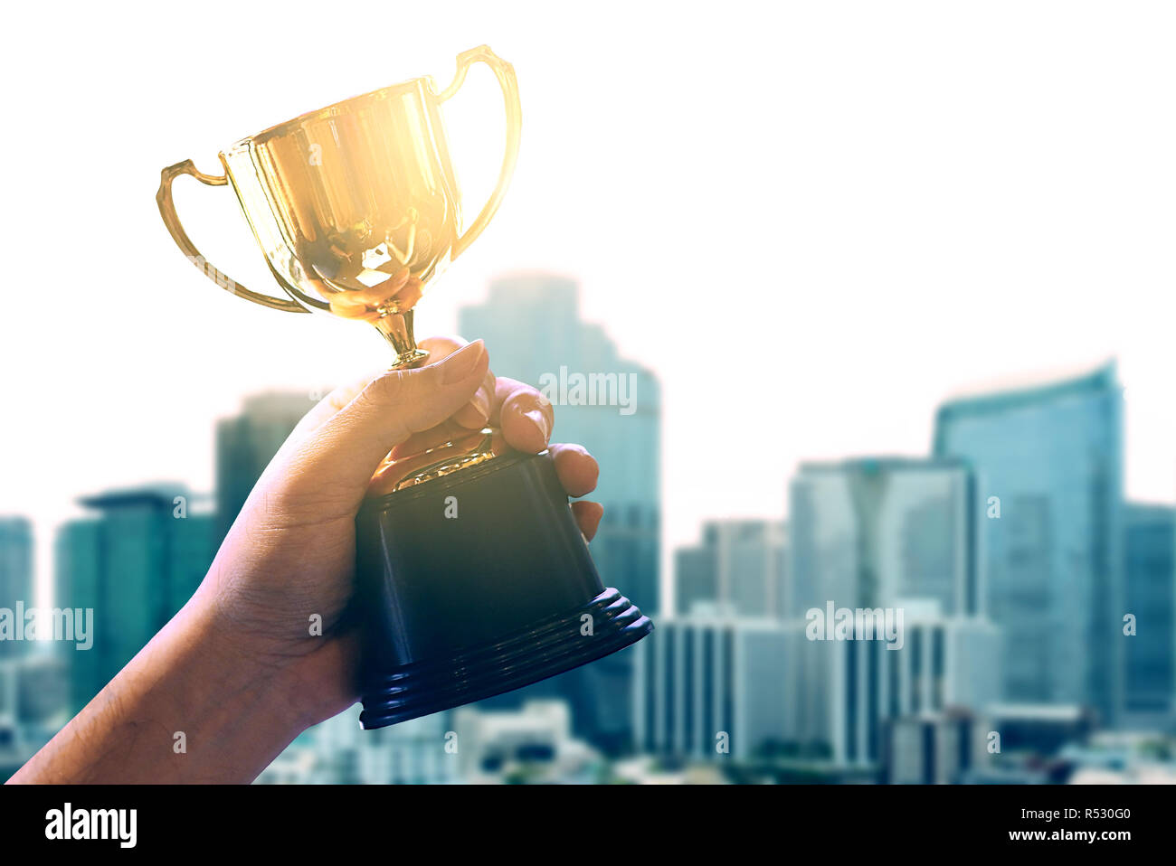 Trophy on winner hand with blur background business tower and sun flare ...