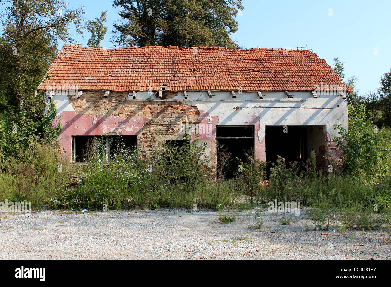 Abandoned small red brick family house with facade and roof tiles destroyed during war and ...