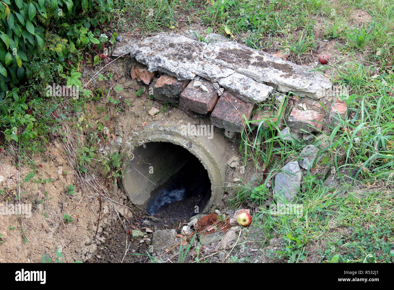 Concrete sewer pipe exit covered with dirt, red bricks and broken ...