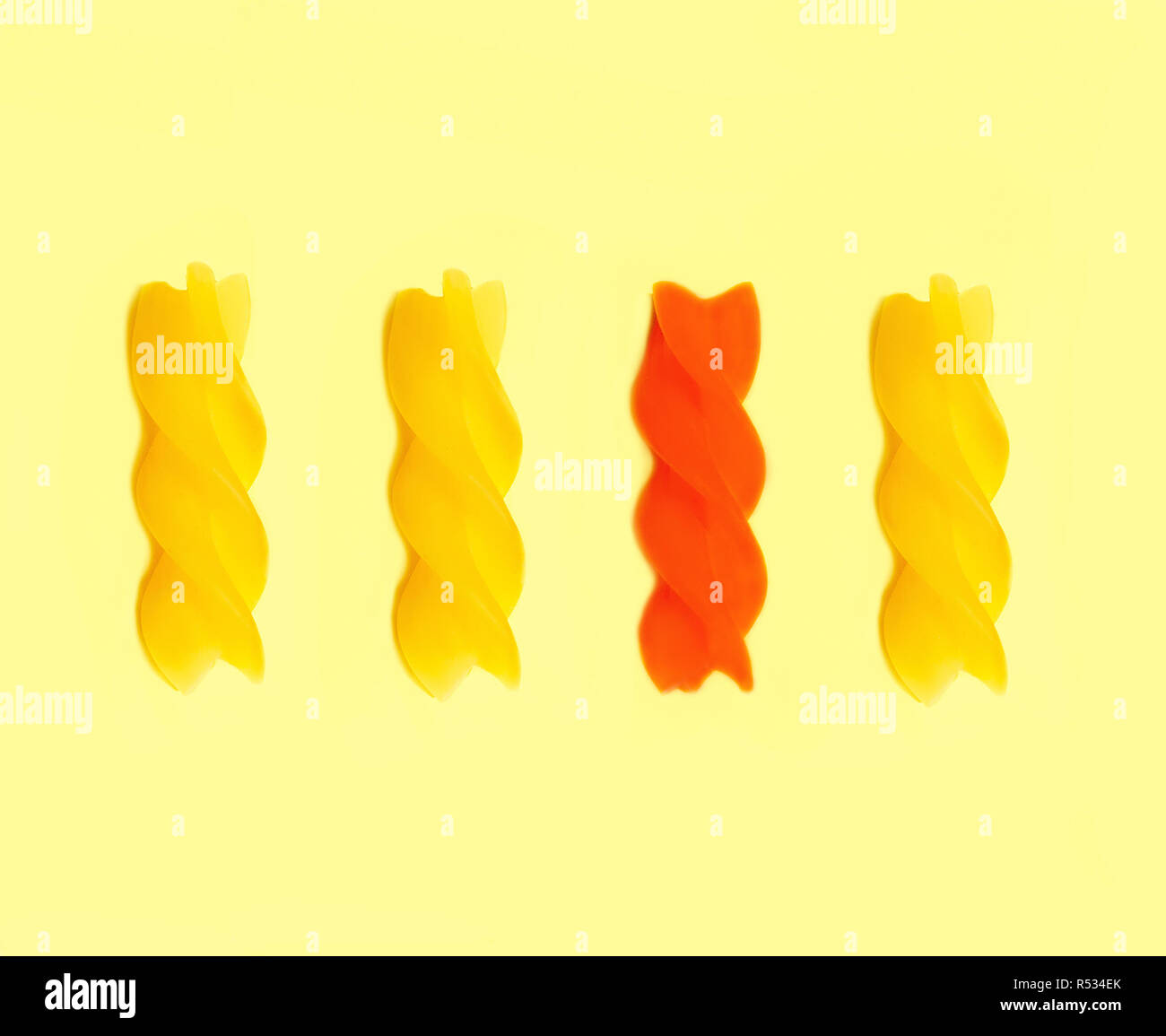 Four multicolor raw fusilli pasta in a row isolated on light yellow ...