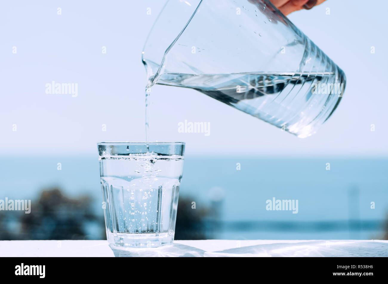 Pure water from a jug is poured into a glass beaker. Glass with water ...