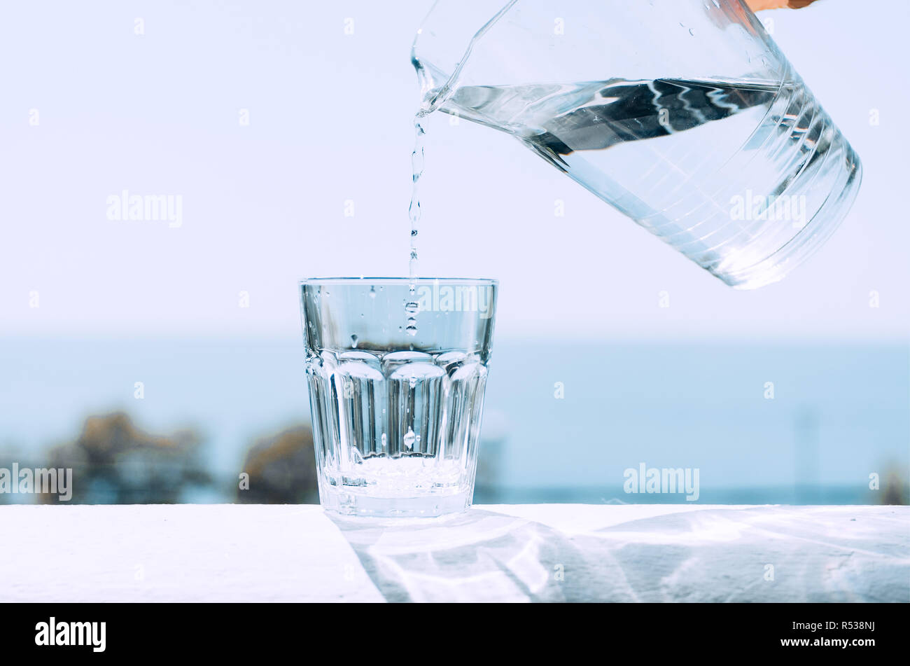Pure water from a jug is poured into a glass beaker. Glass with water ...