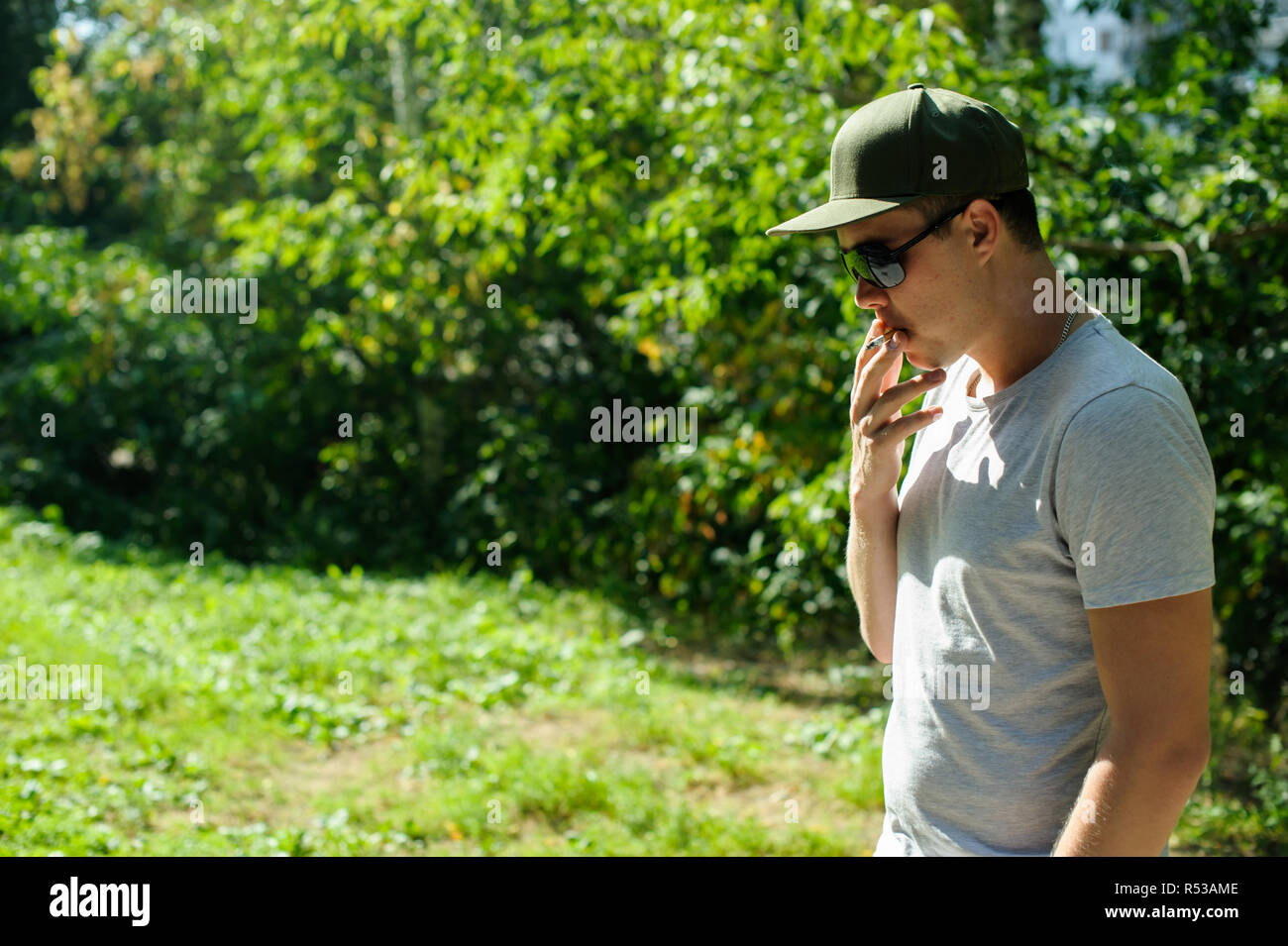a young man dressed in light and dark ftbolku cap, smoking a cigarette ...