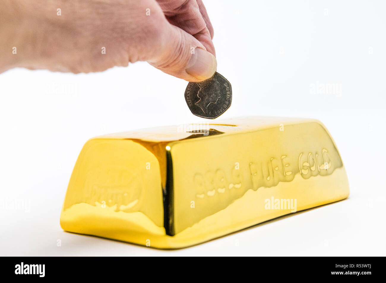 Human hand putting a 50 pence coin into a money box shaped like a Gold ...