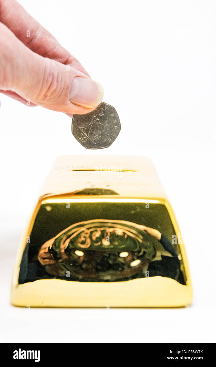 Human hand putting a 50 pence coin into a money box shaped like a Gold ...