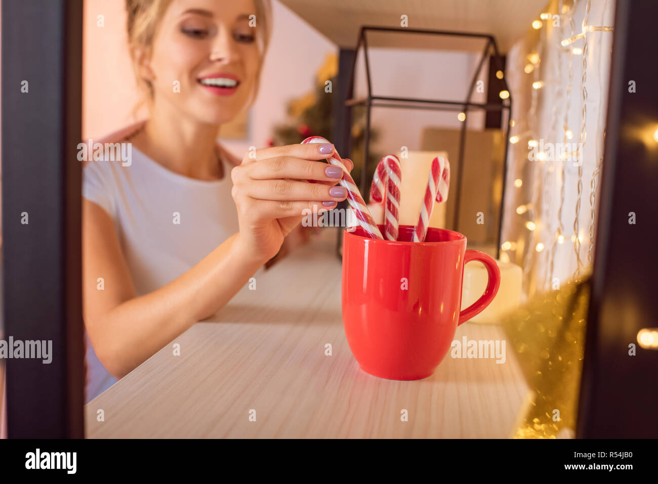 smiling young blonde woman putting candy canes in red cup at christmas ...