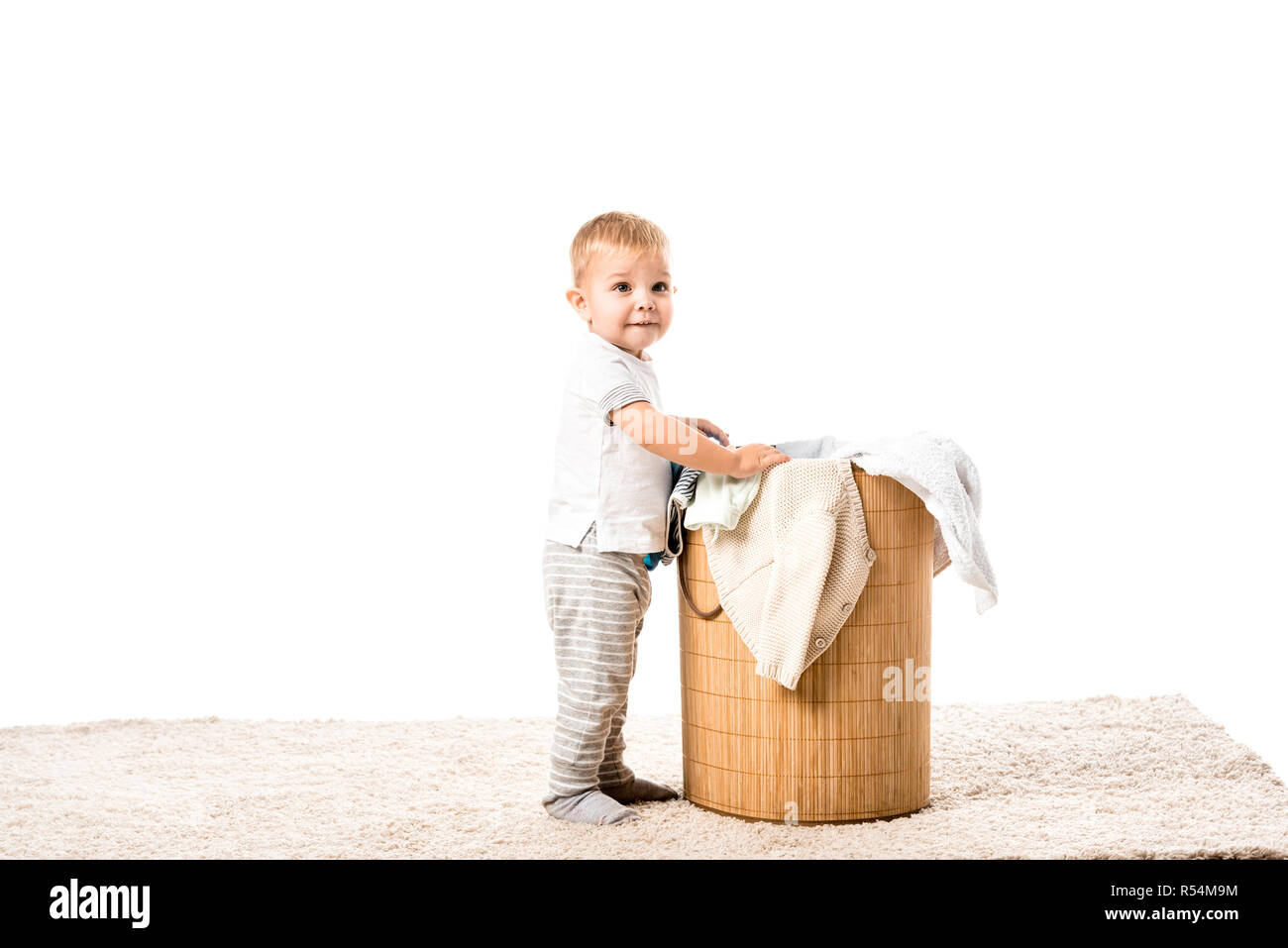 toddler boy standing in front of wicker laundry basket and smiling ...