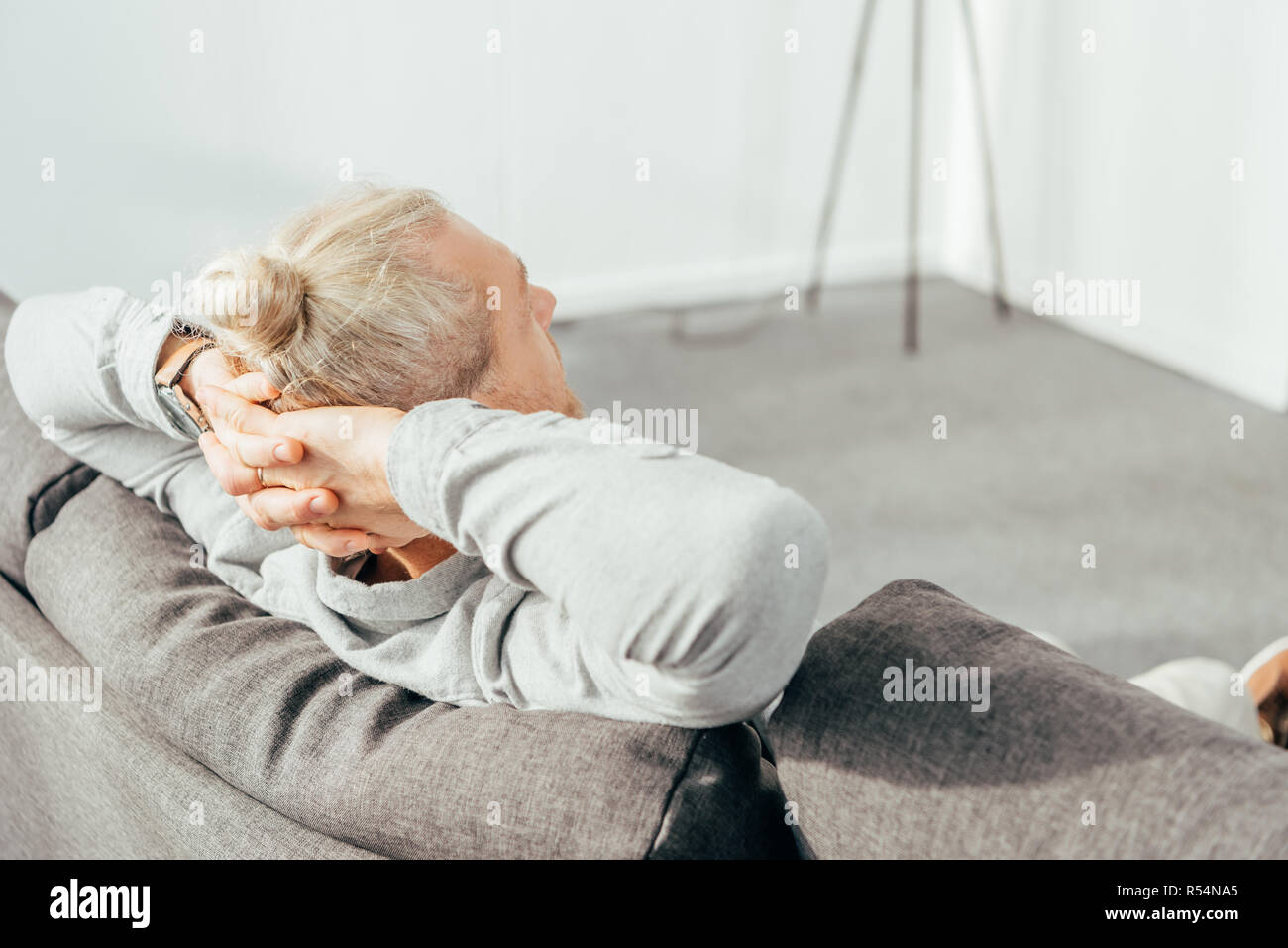 back view of man resting with hands behind head on couch Stock Photo ...