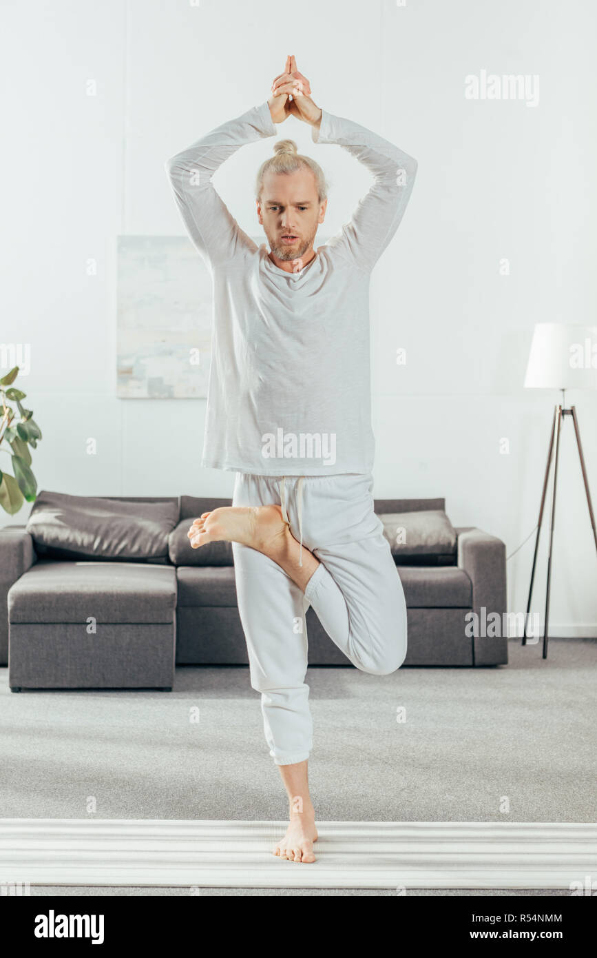 full length view of man standing in tree pose on yoga mat at home Stock ...
