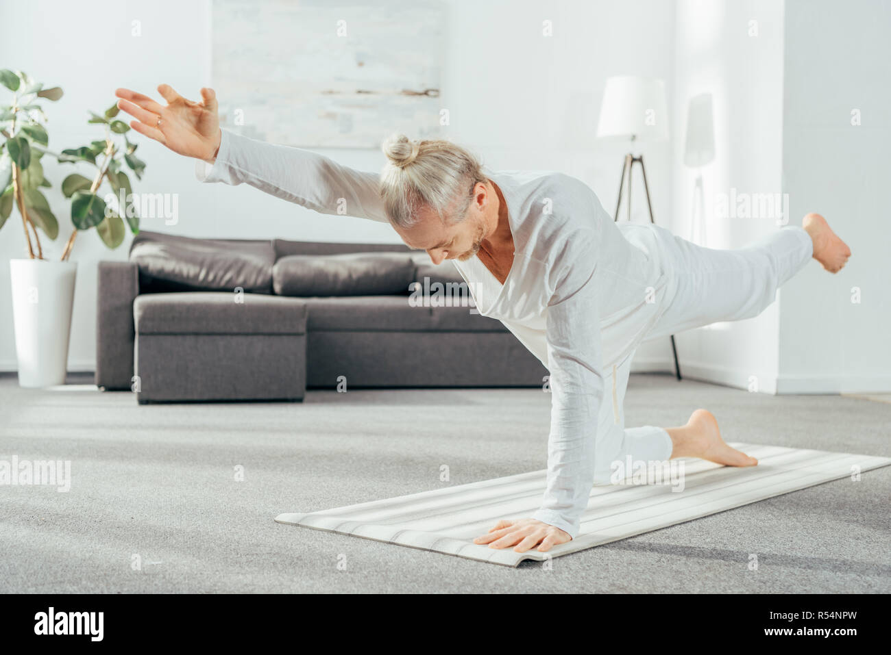 man standing in Balancing the Cat pose on yoga mat at home Stock Photo ...