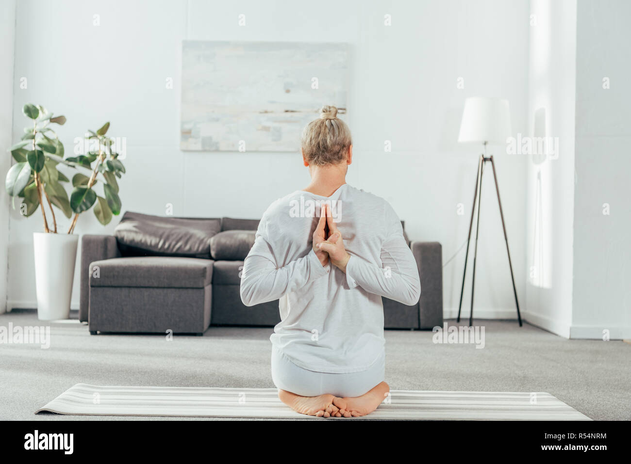 back view of man sitting in yoga pose with hands behind back at home ...