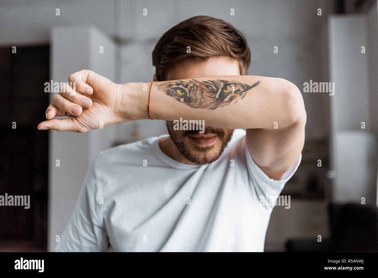 handsome young man covering face with arm with tattooed tiger eyes at ...