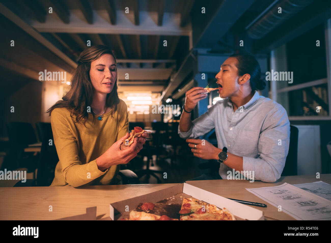 business colleagues eating pizza sitting together in office late in the ...