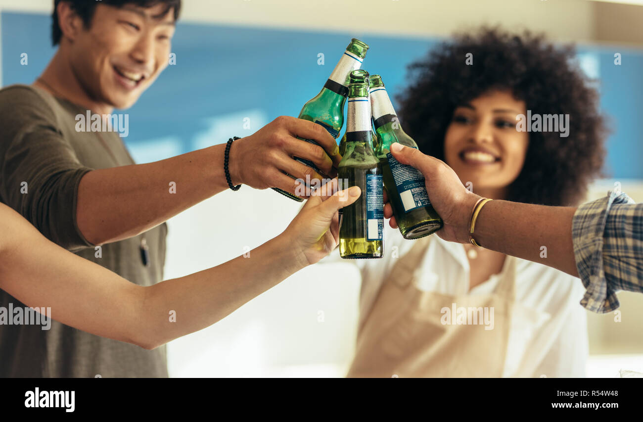 Four friends toasting beer standing together at home. Multiethnic ...