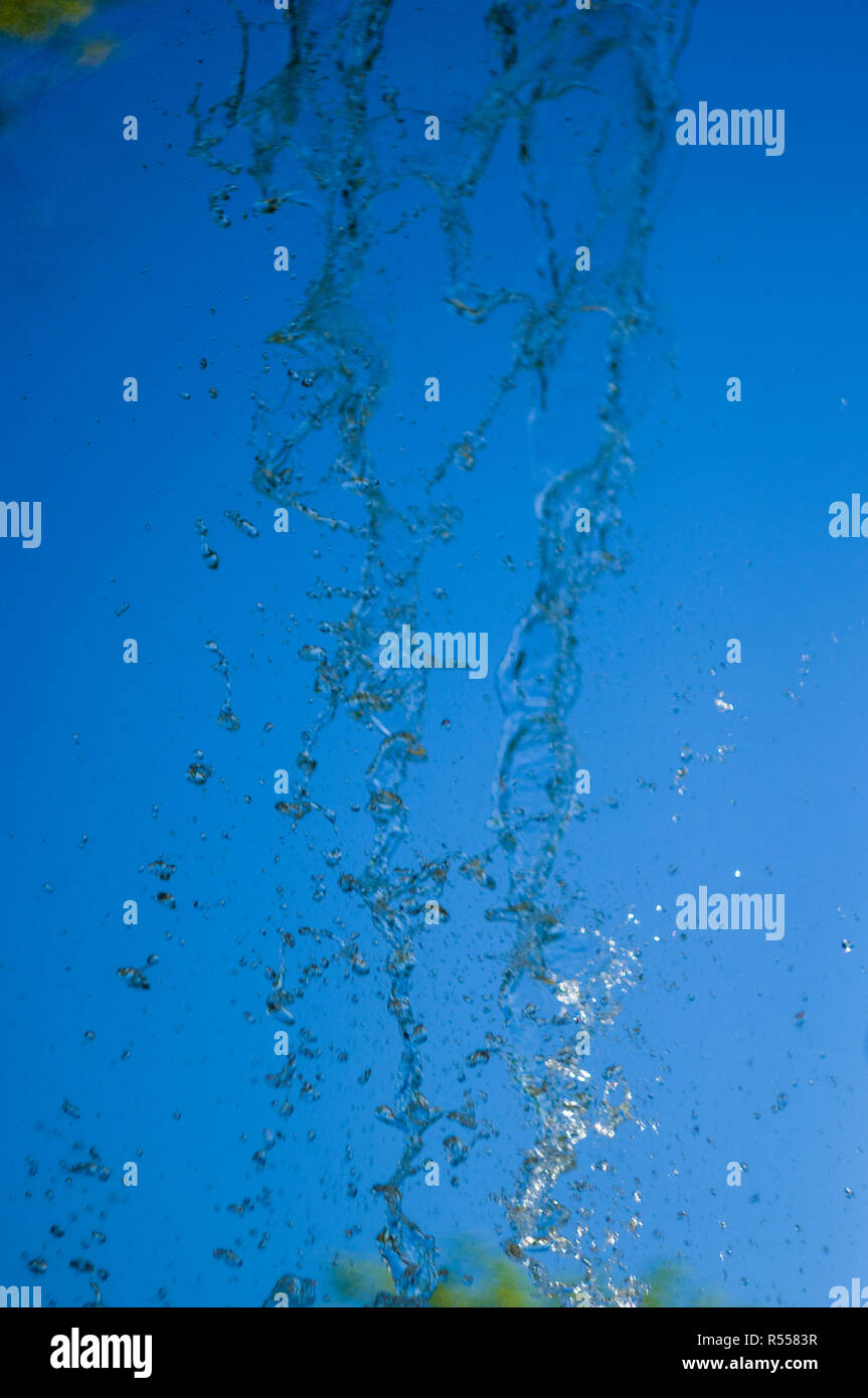 transparent falling water vertical flows against a blue sky and green ...