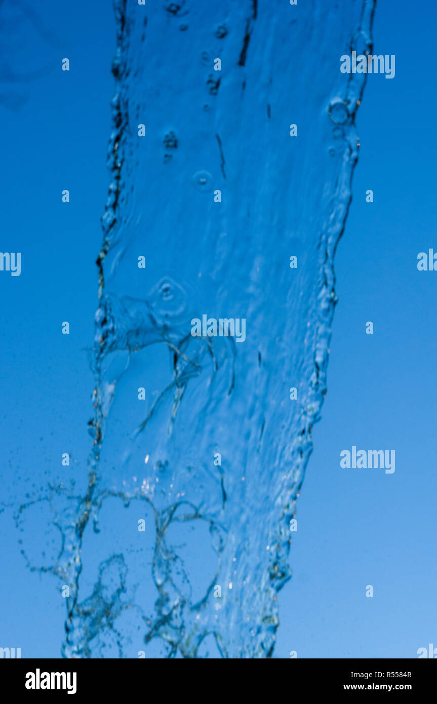transparent falling water vertical flows against a blue sky and green ...
