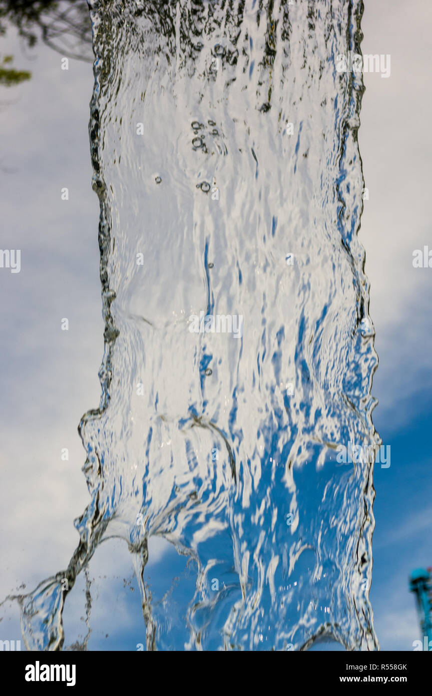 transparent falling water vertical flows against a blue sky and green ...