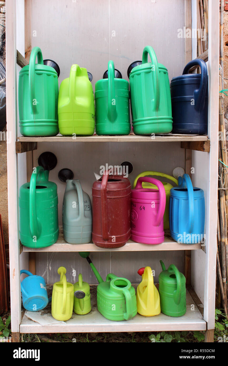 Plastic watering cans piled on kitchen garden shelves Stock Photo - Alamy