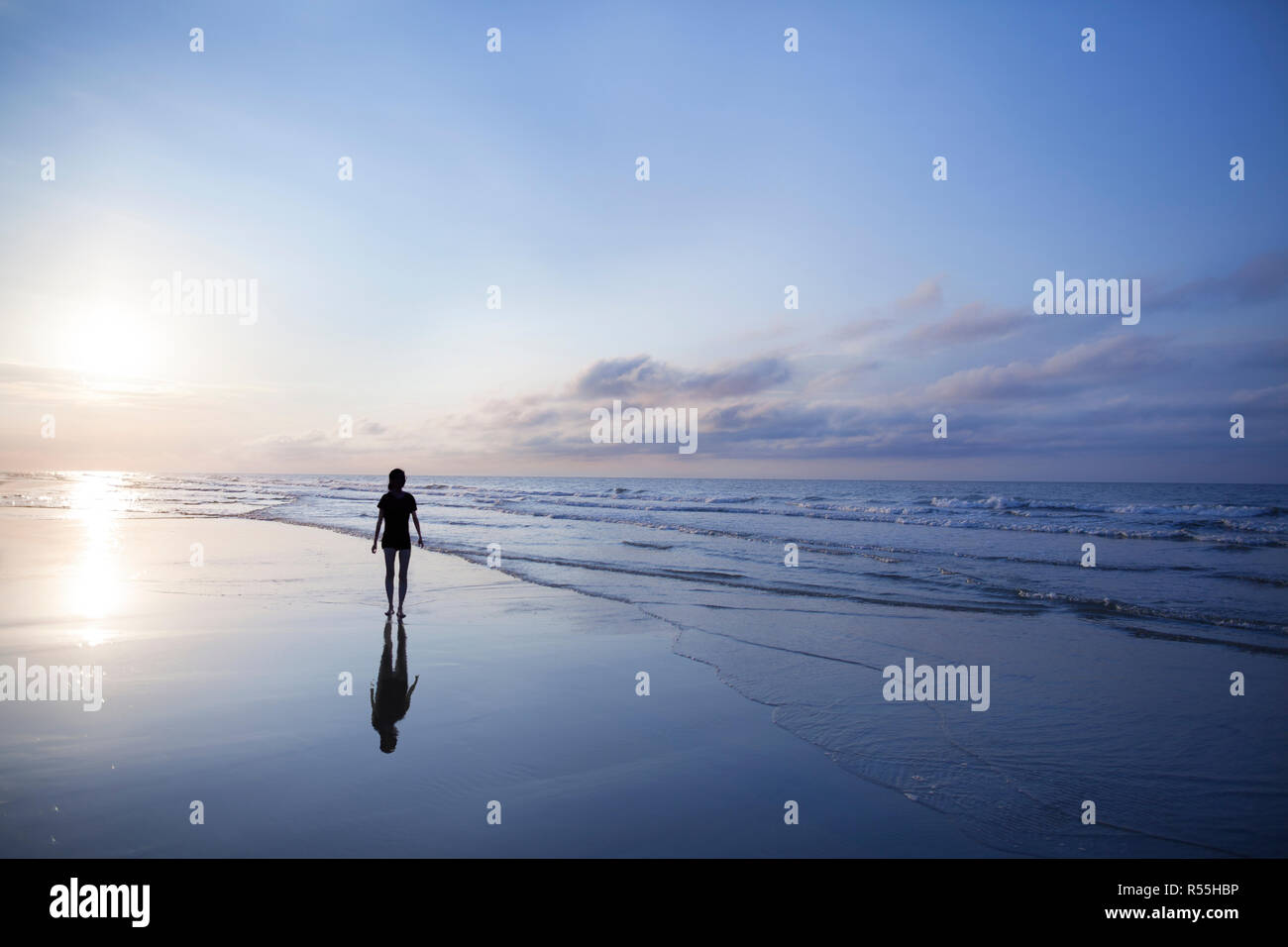 Woman walking on beach at sunrise Stock Photo - Alamy