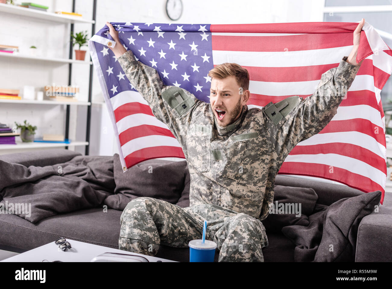 excited army soldier sitting on couch, cheering and proudly holding ...