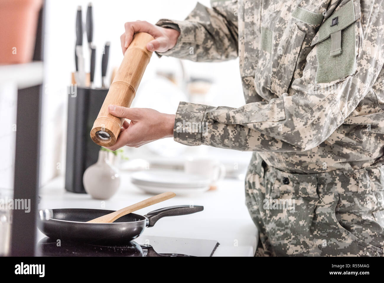 cropped view of army soldier using pepper pot while cooking in kitchen ...