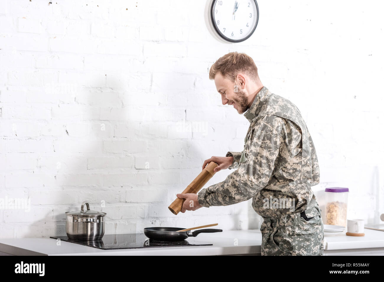 smiling army soldier using pepper pot while cooking in kitchen Stock ...
